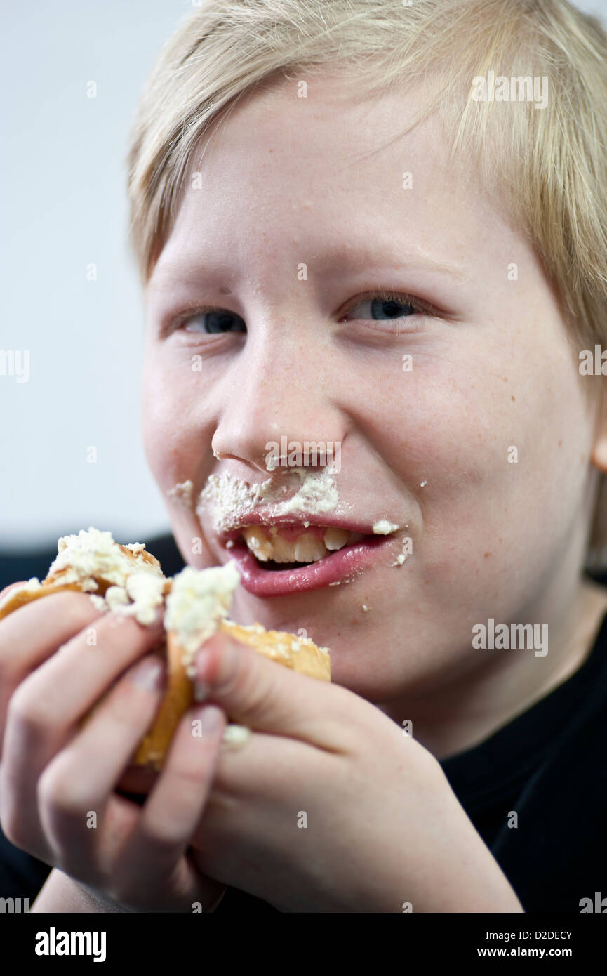 Young boy eating cream bun getting whipped cream all over his face ...