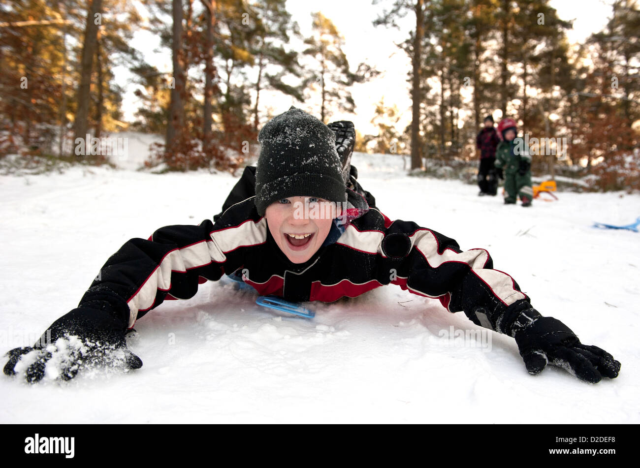Young boy gliding on his belly in the snow Stock Photo - Alamy