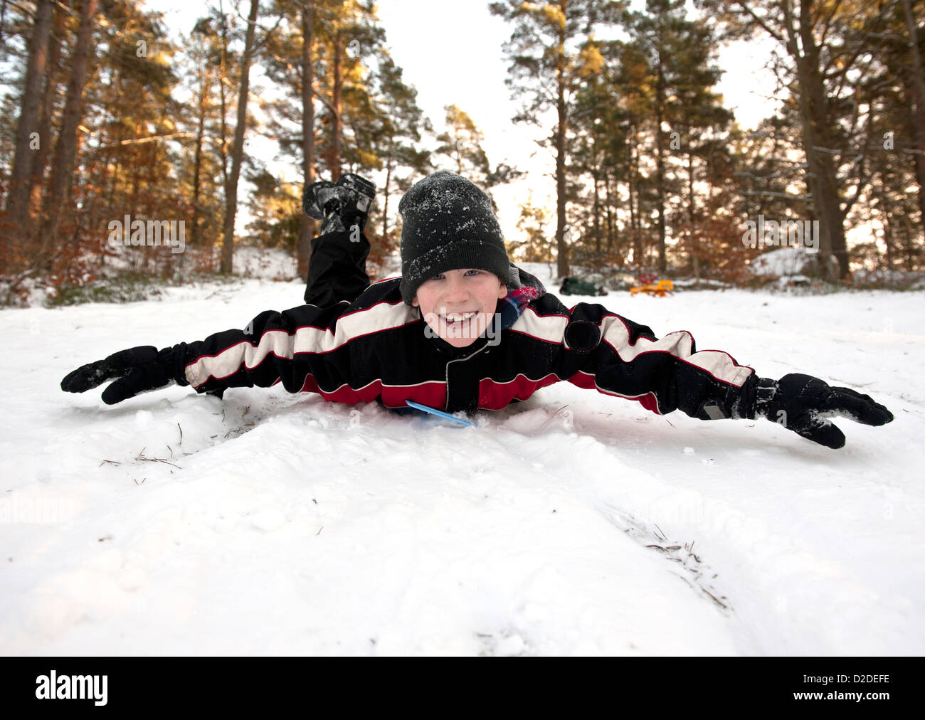 Young boy gliding on his belly in the snow Stock Photo - Alamy