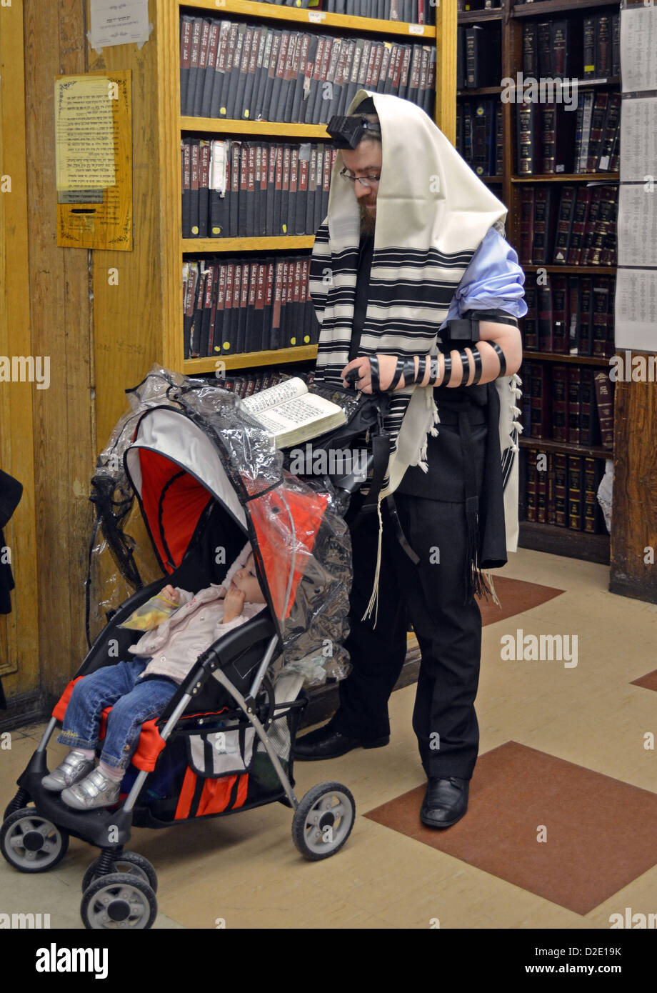 Rabbi praying while leaning his prayer book on daughter's carriage at ...