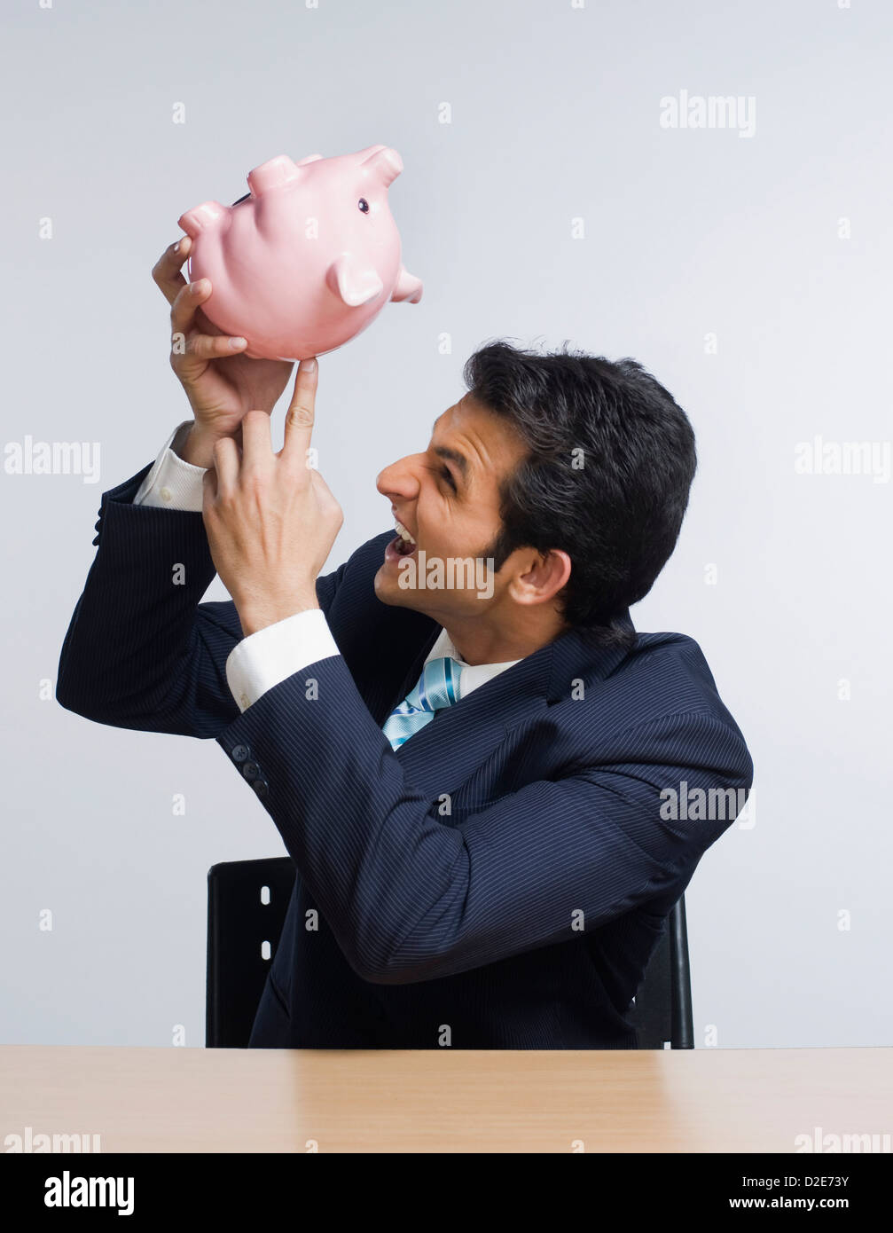 Businessman looking angry while emptying a piggy bank Stock Photo - Alamy