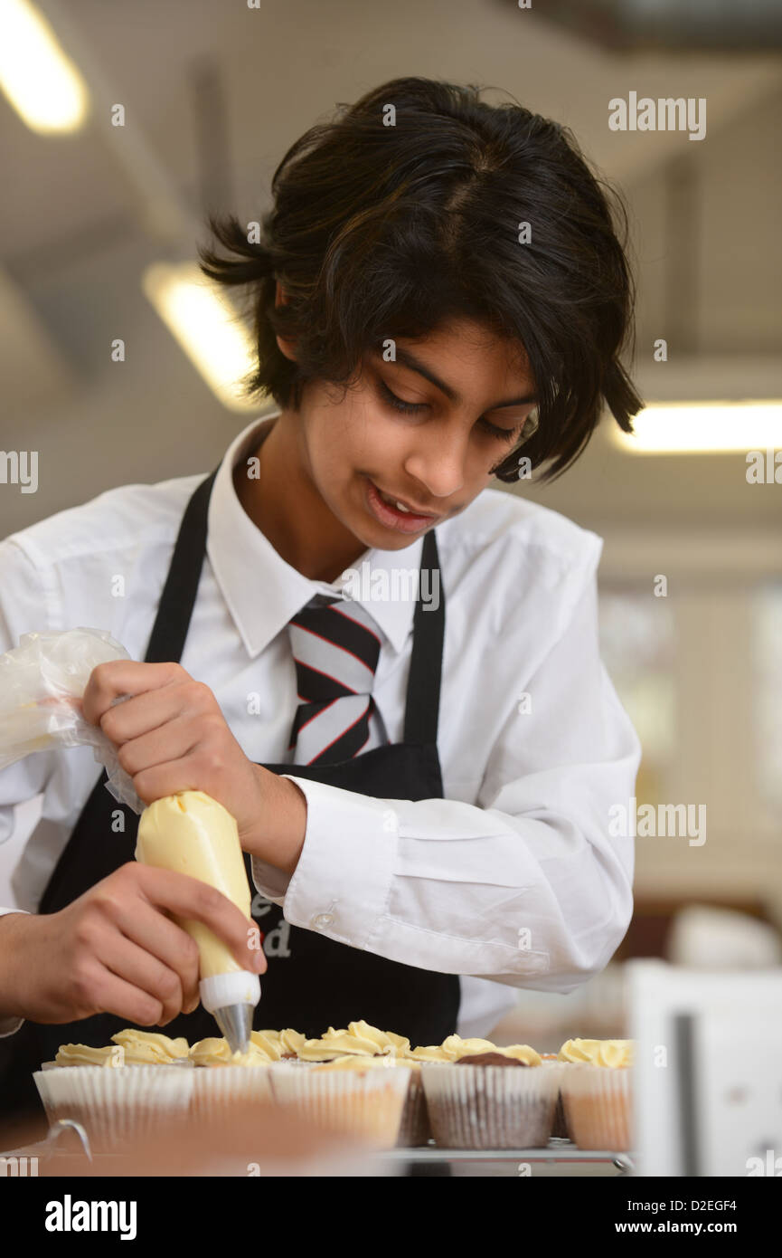 A schoolgirl using an icing bag to top cupcakes during a food Science ...