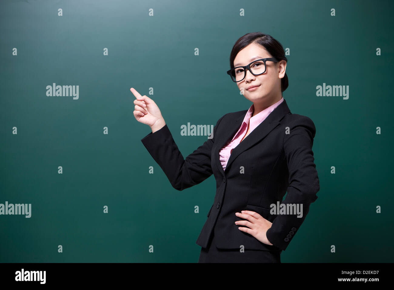 Serious female teacher pointing to blackboard in classroom Stock Photo ...
