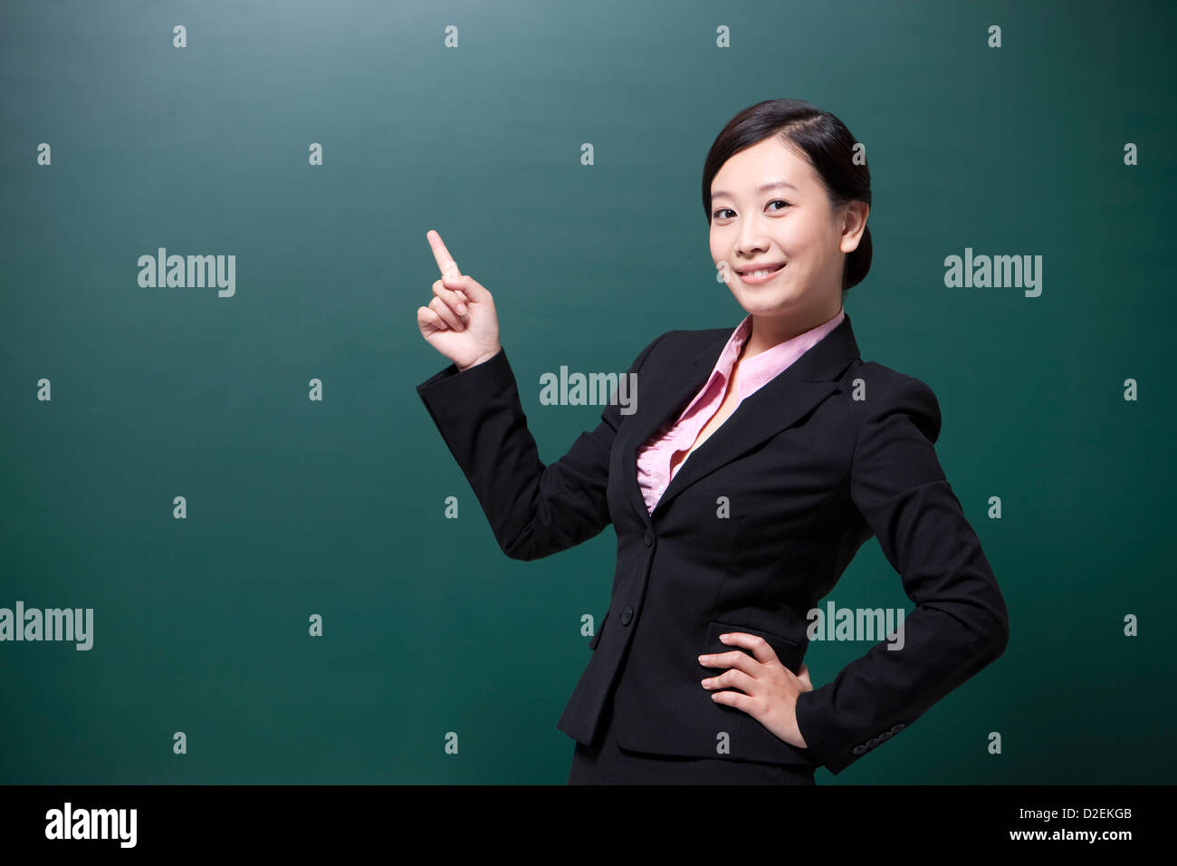 Smiling female teacher pointing to blackboard in classroom Stock Photo ...