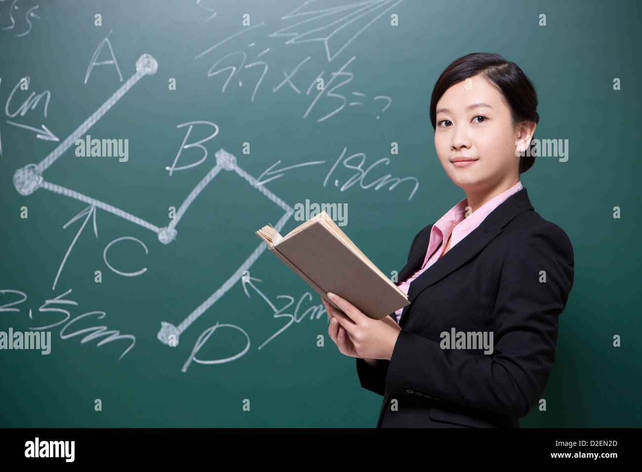 Serious female teacher holding textbooks in classroom Stock Photo - Alamy