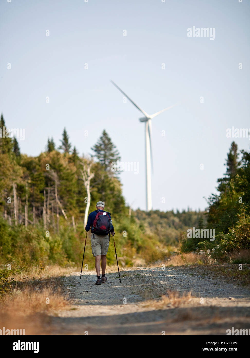 A man hikes along a trail with a wind turbine looming in the background ...