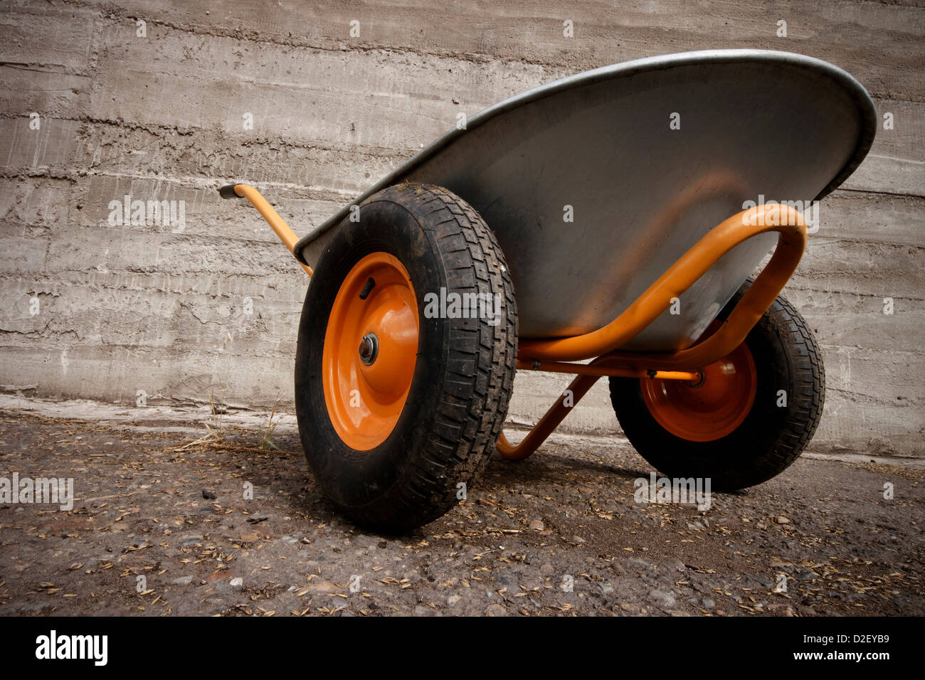 Orange wheelbarrow on concrete background Stock Photo - Alamy