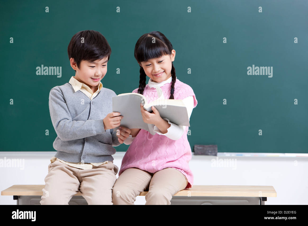 Happy schoolchildren reading a book together in classroom Stock Photo ...