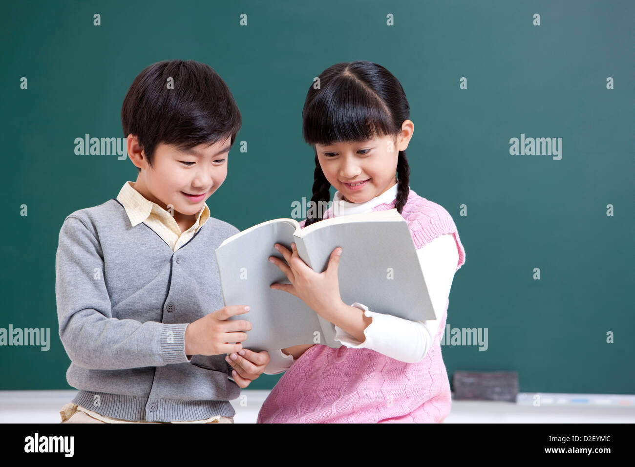 Happy schoolchildren reading a book together in classroom Stock Photo ...