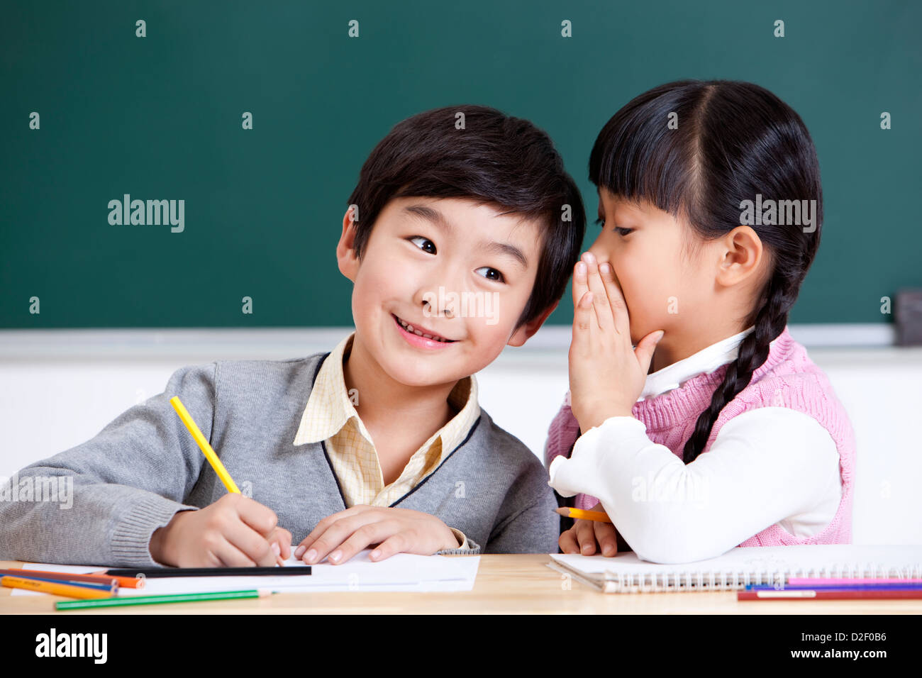 Cheerful schoolchildren whispering in classroom Stock Photo - Alamy