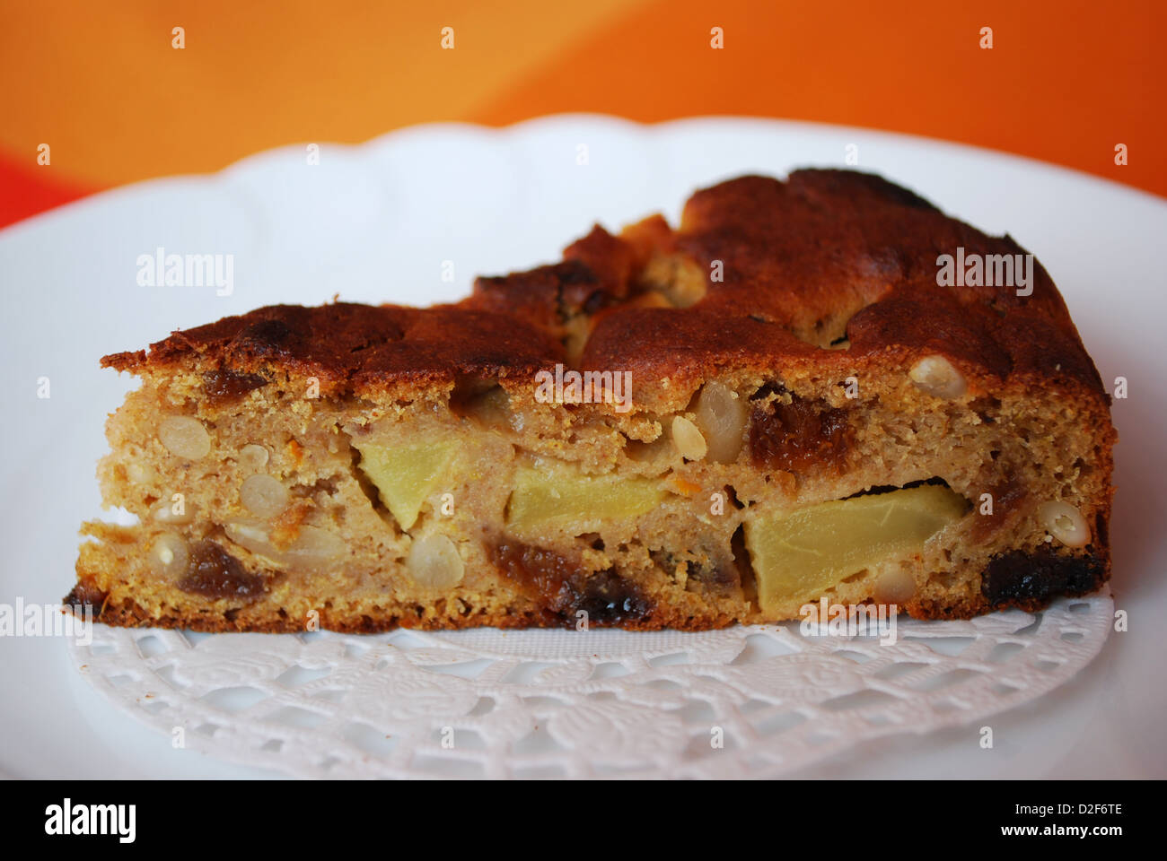 Closeup of a slice of an apple pie on white dish and orange background ...