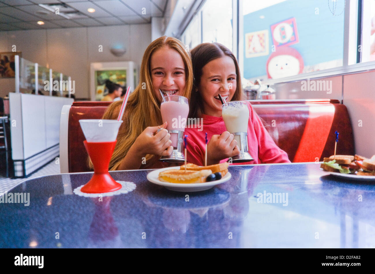 Teenage girls in diner, eating french fries, milkshakes, laughing ...