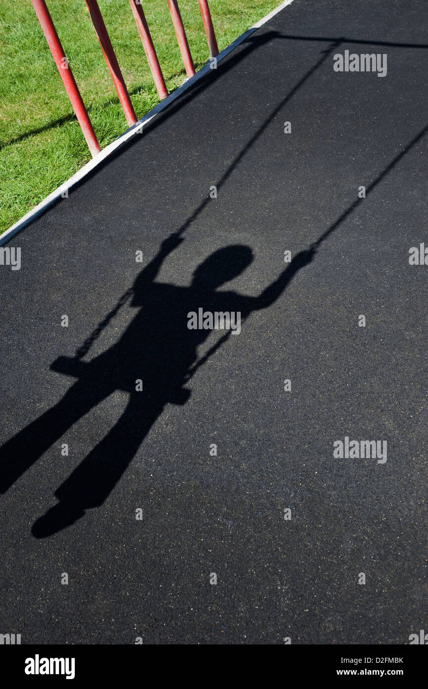 Shadow cast by a young child playing on a swing in a children’s ...