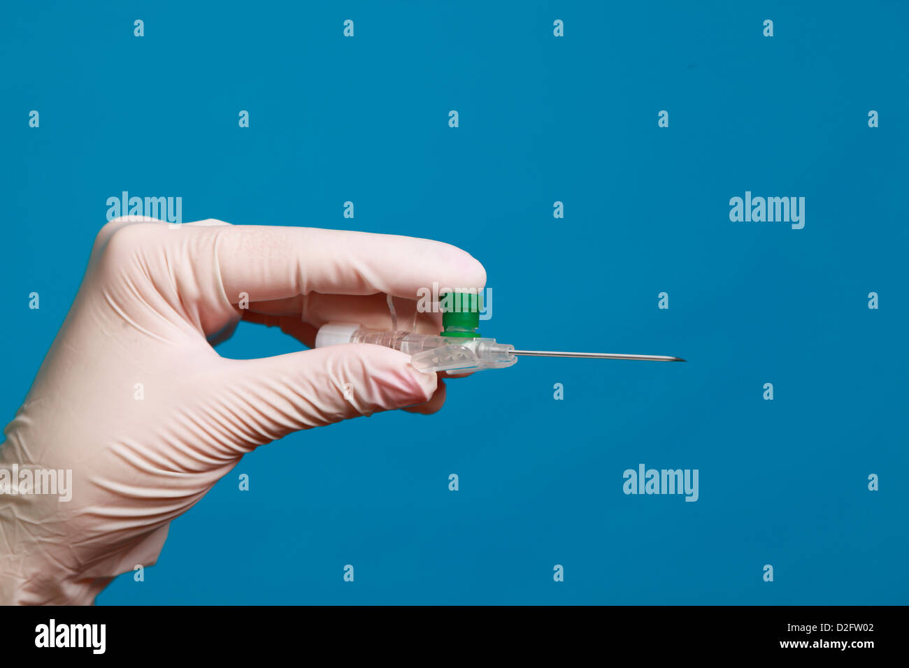 Hand in surgical glove holding a small intravenous needle against a ...