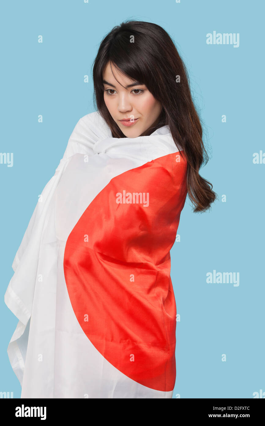Patriotic Young Woman Wrapped In Japanese Flag Over Blue Background