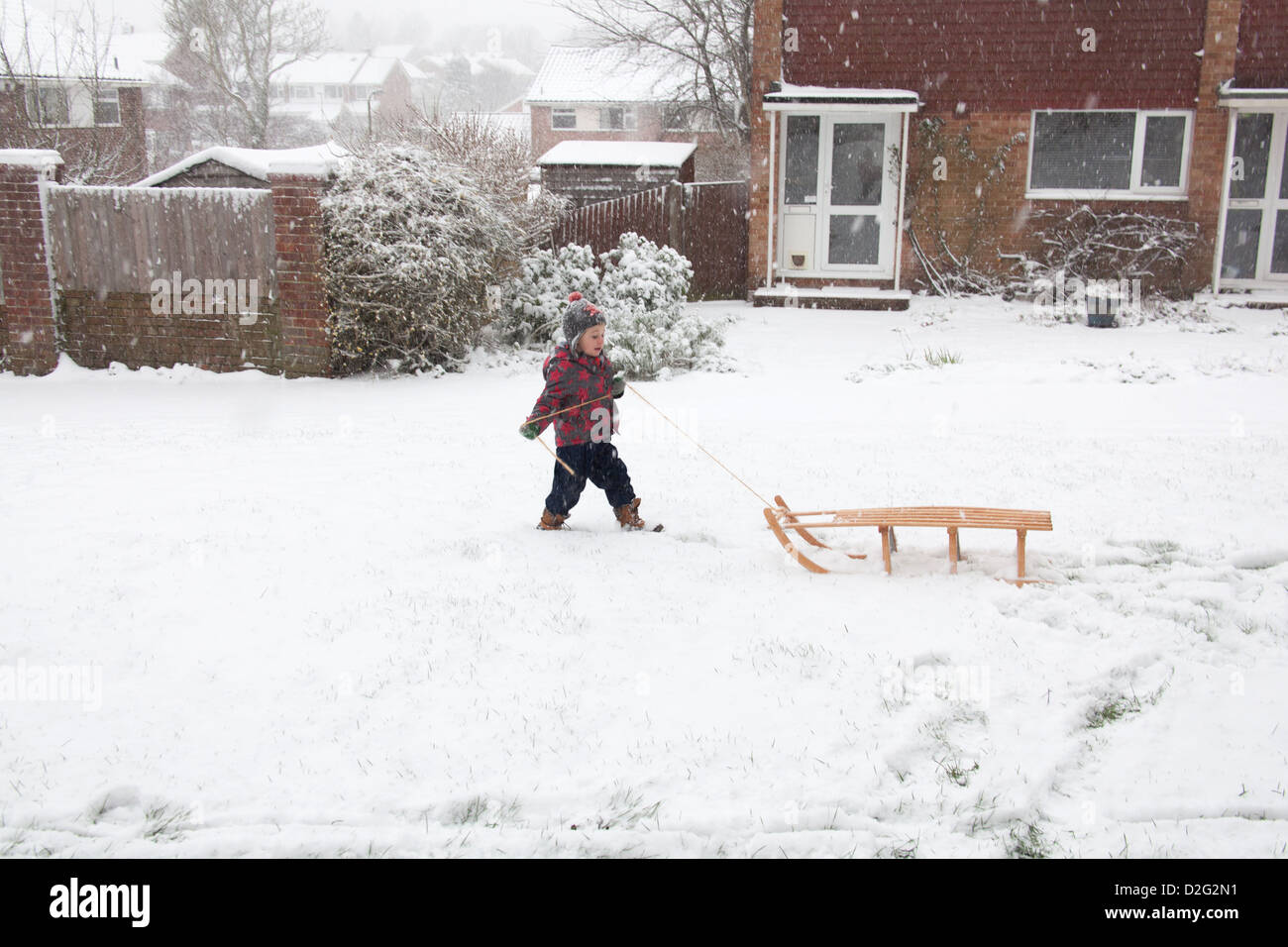 Three year old boy outside playing in the snow on a toboggan. Alresford ...