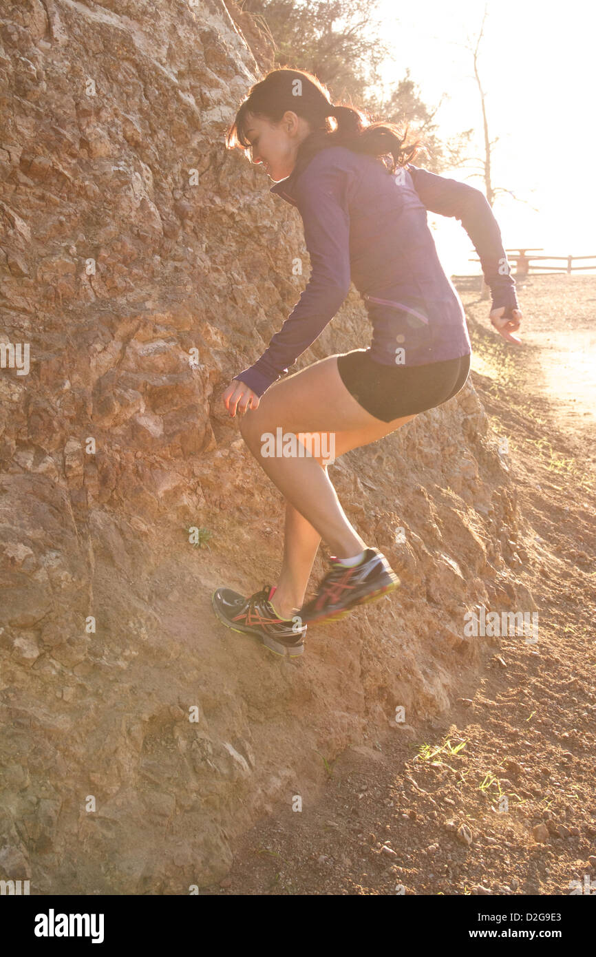 A determined woman practices trail running and climbs a steep rock face ...