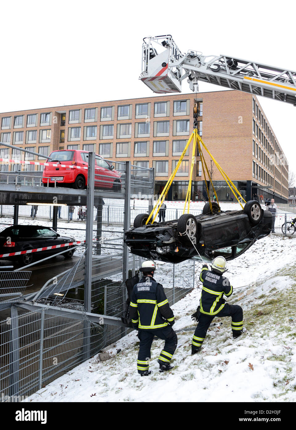Firemen lift an upside down car off the ground next to a parking garage ...