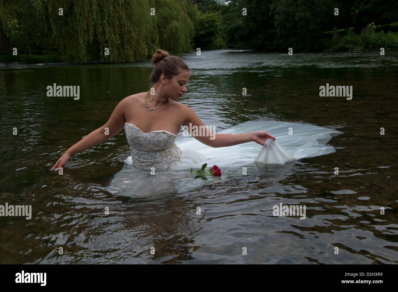 young lady in white wedding dress watching roses float away down stream ...