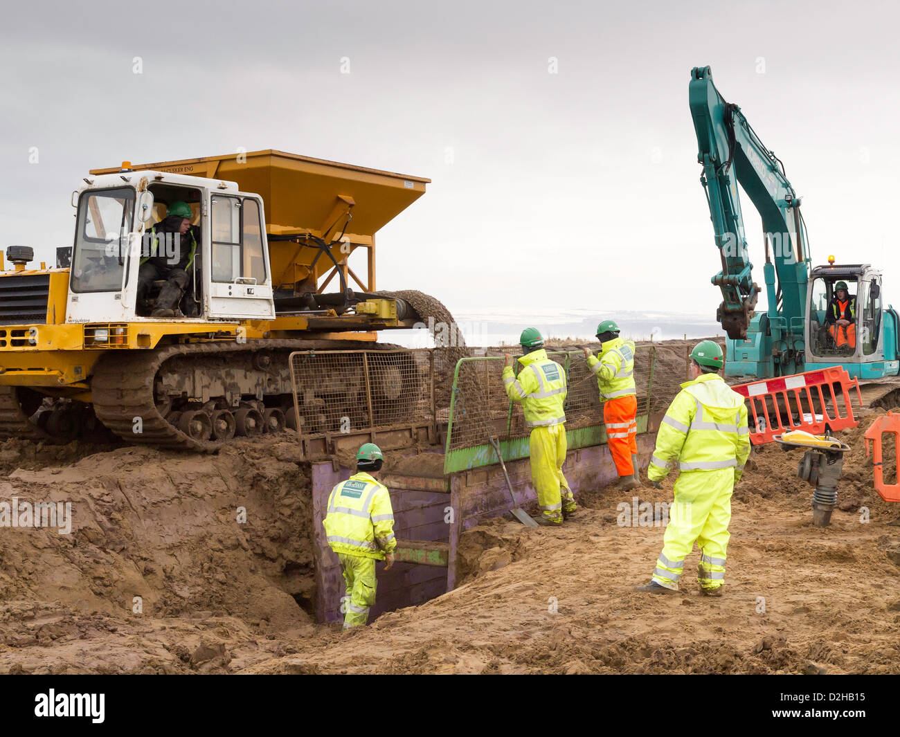 Workmen laying a replacement sewage pipeline using a tracked dumper ...
