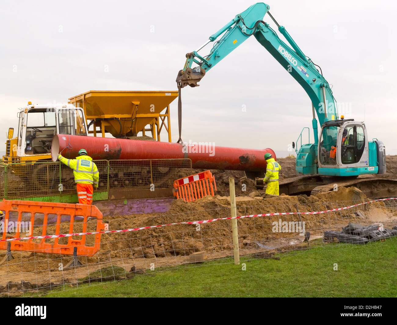 Workmen laying a replacement sewage pipeline using an excavator to lift ...