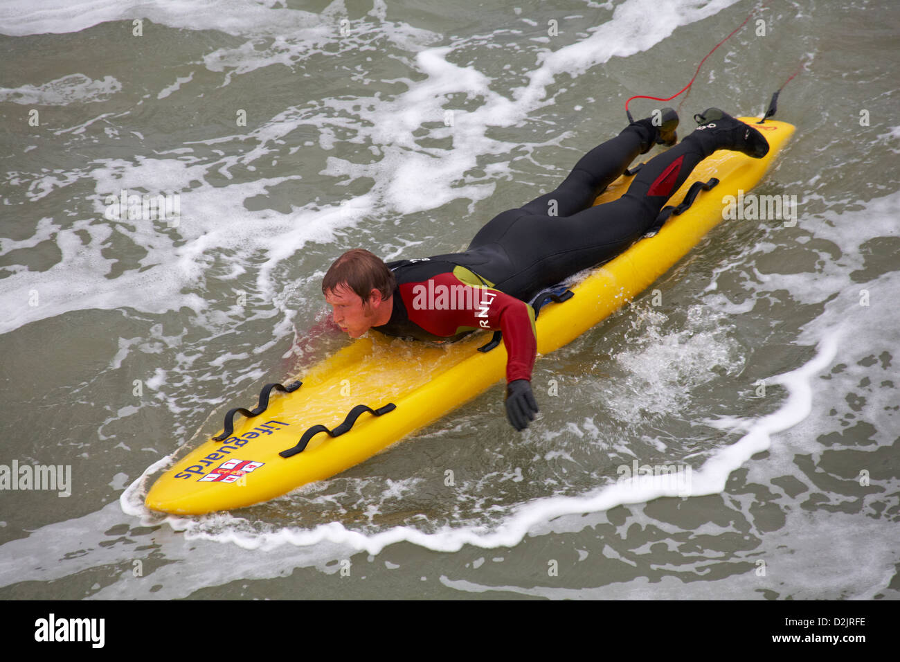 RNLI Lifeguard surfing on surfboard in the sea at Boscombe, Dorset UK ...