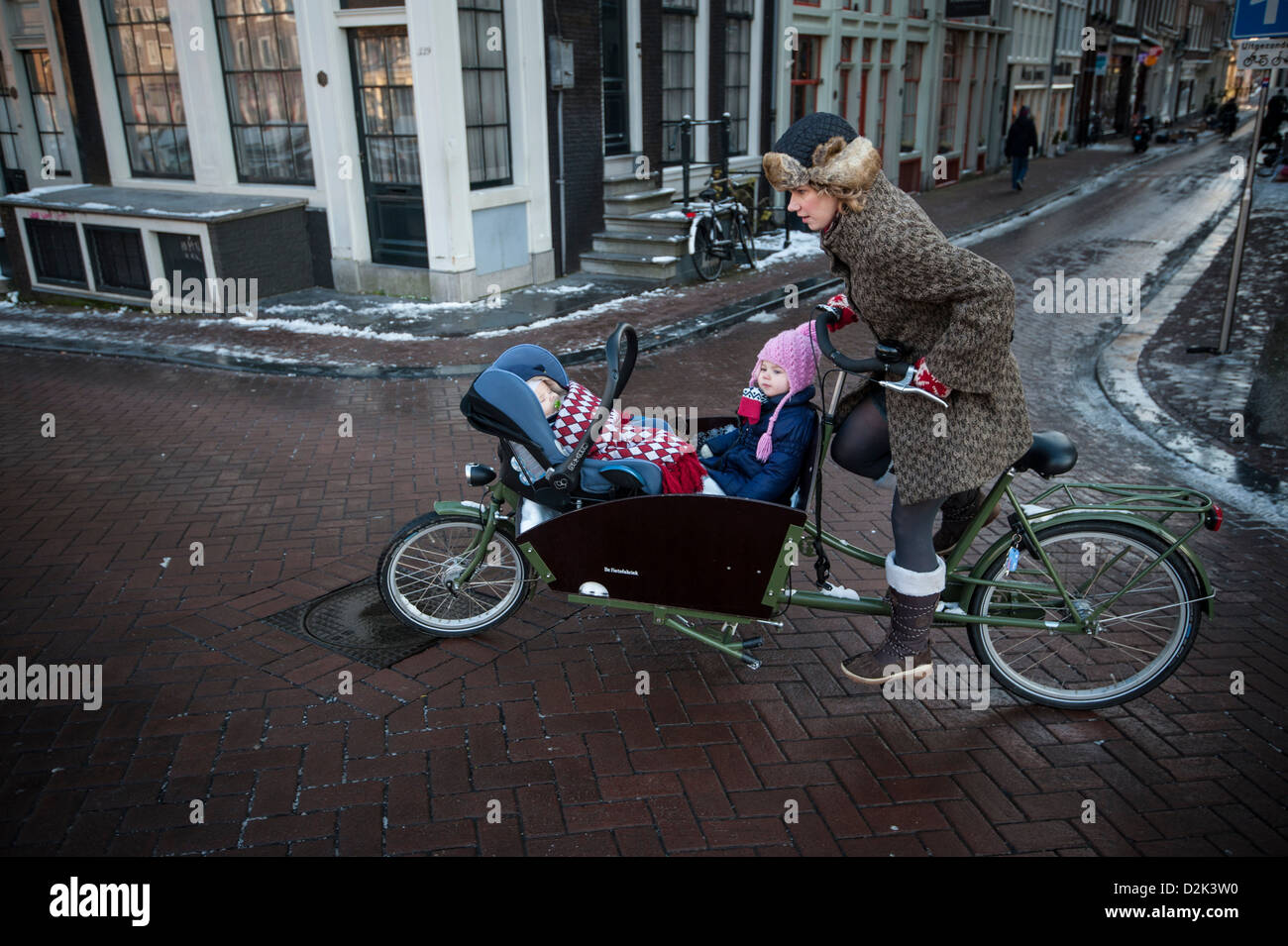 Mother with two kids in bicycle front navigating a slippery winter road ...