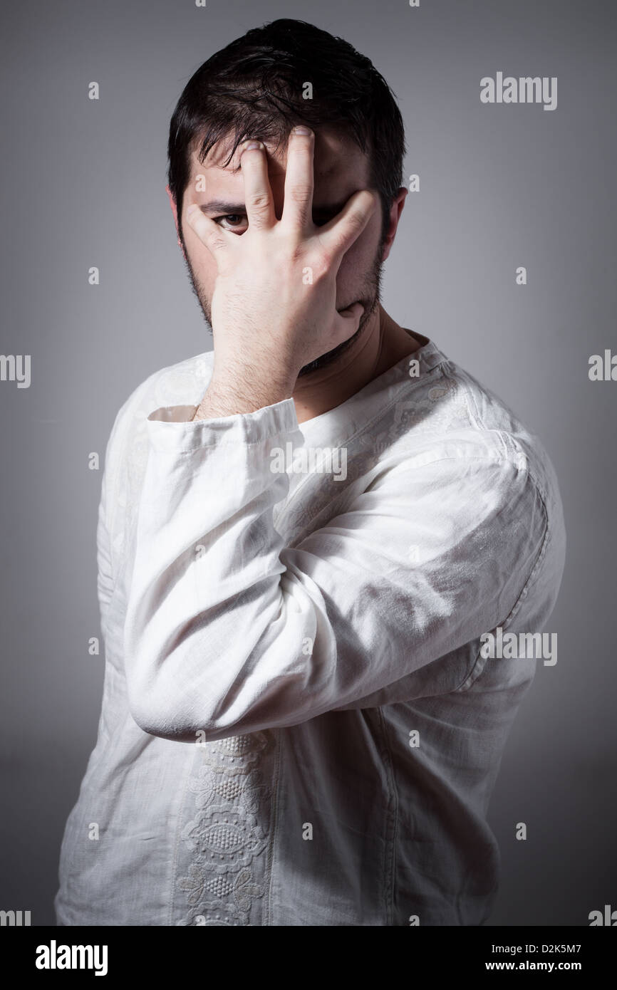 Young man hiding his face with a hand while looking through fingers ...