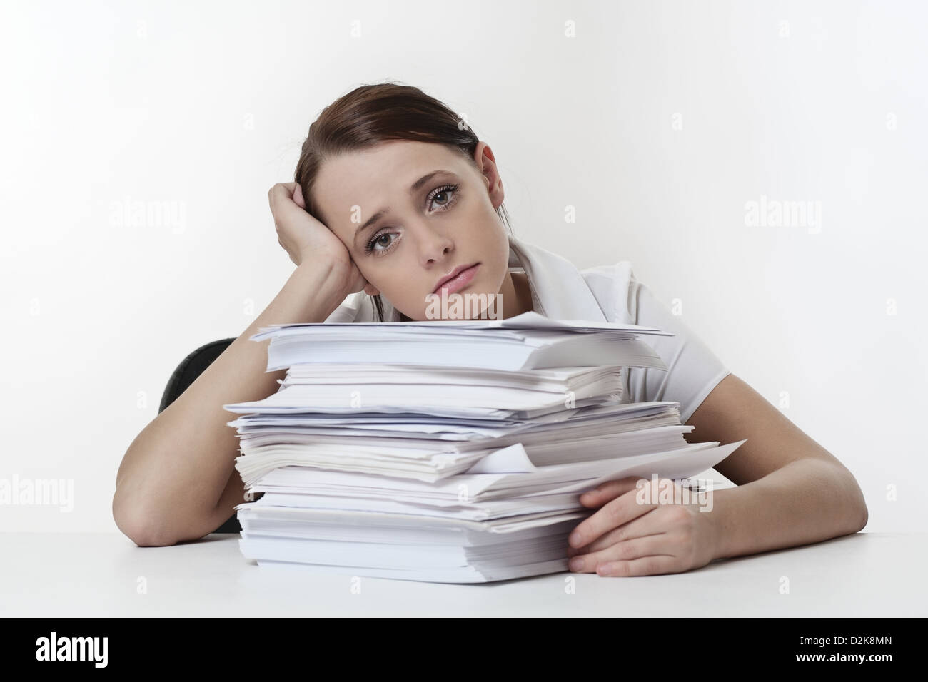 A stressed female, sitting at her desk with a large pile of papers ...