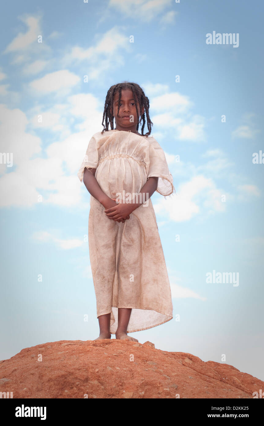 Young Ethiopian girl standing on top of mound, with sky behind her ...