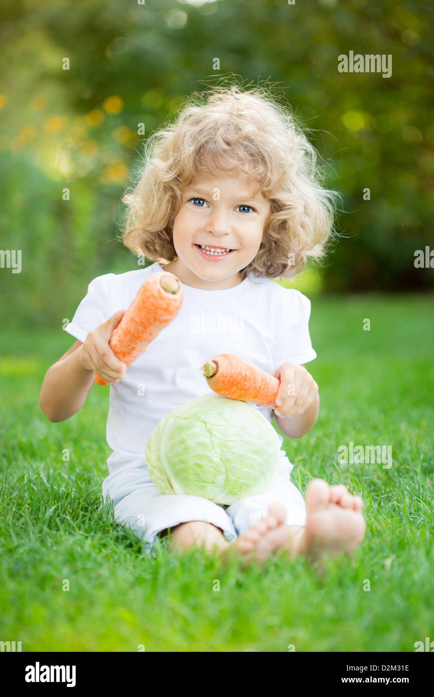 Happy smiling child with vegetables sitting on green grass in spring ...