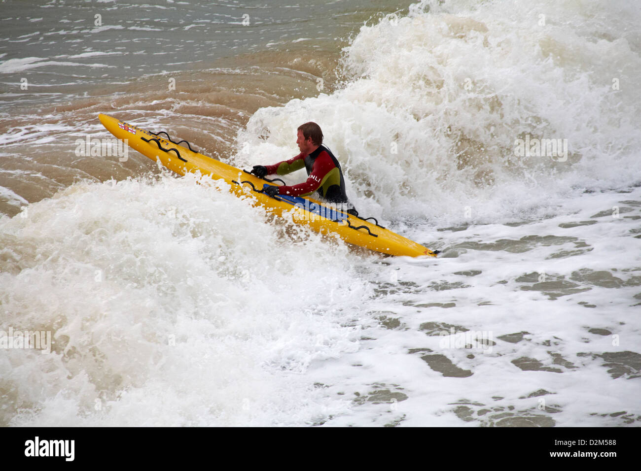 RNLI lifeguard surfing in the sea at Boscombe, Bournemouth, Dorset UK ...