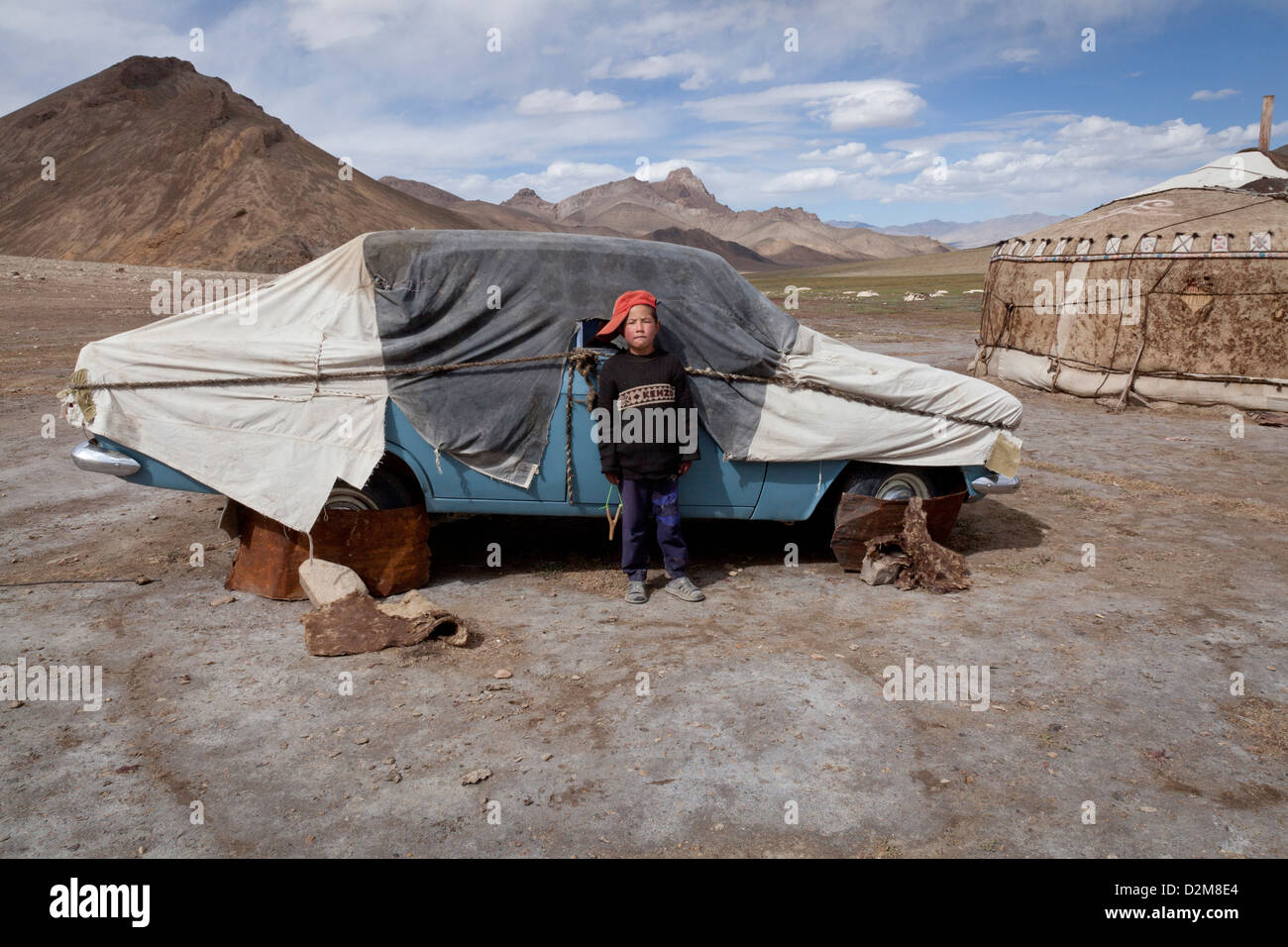 A boy in front of a covered car in a yurt camp in eastern Tajikistan ...