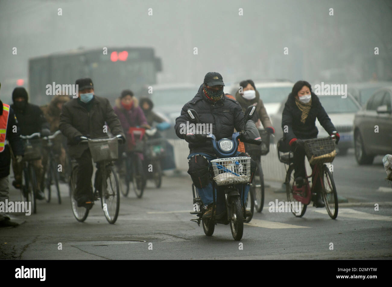 People, some of them wearing the masks, ride bicycles on the street ...