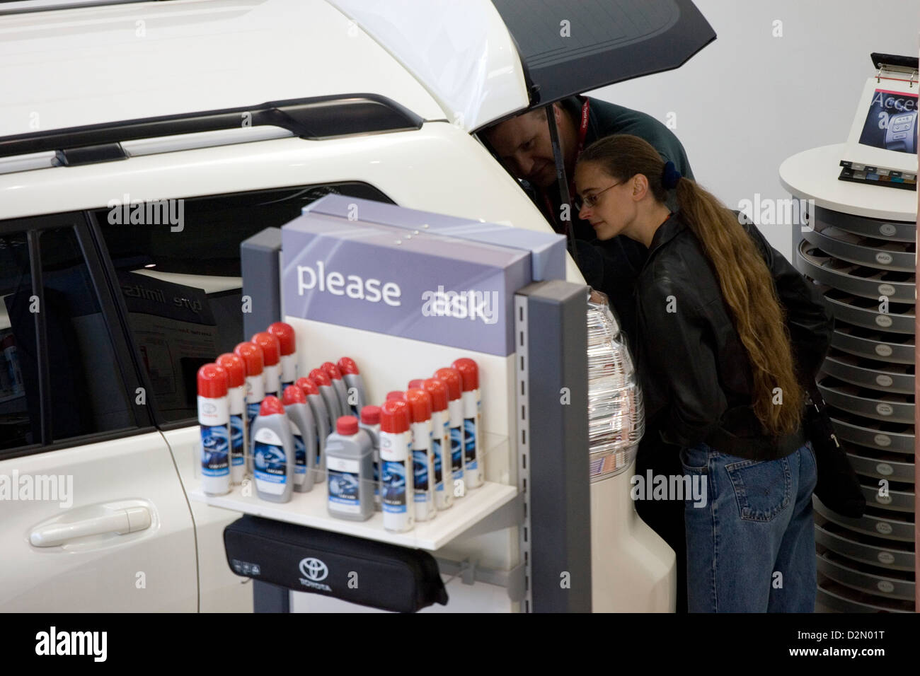 People looking around a car showroom standing next to a please ask sign ...