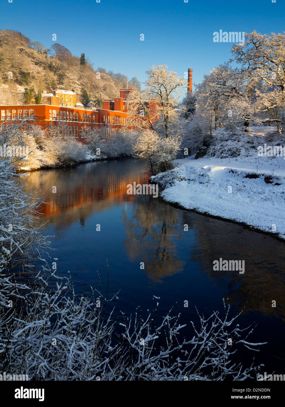 Masson Mill and River Derwent in winter sunshine with snow and blue sky ...