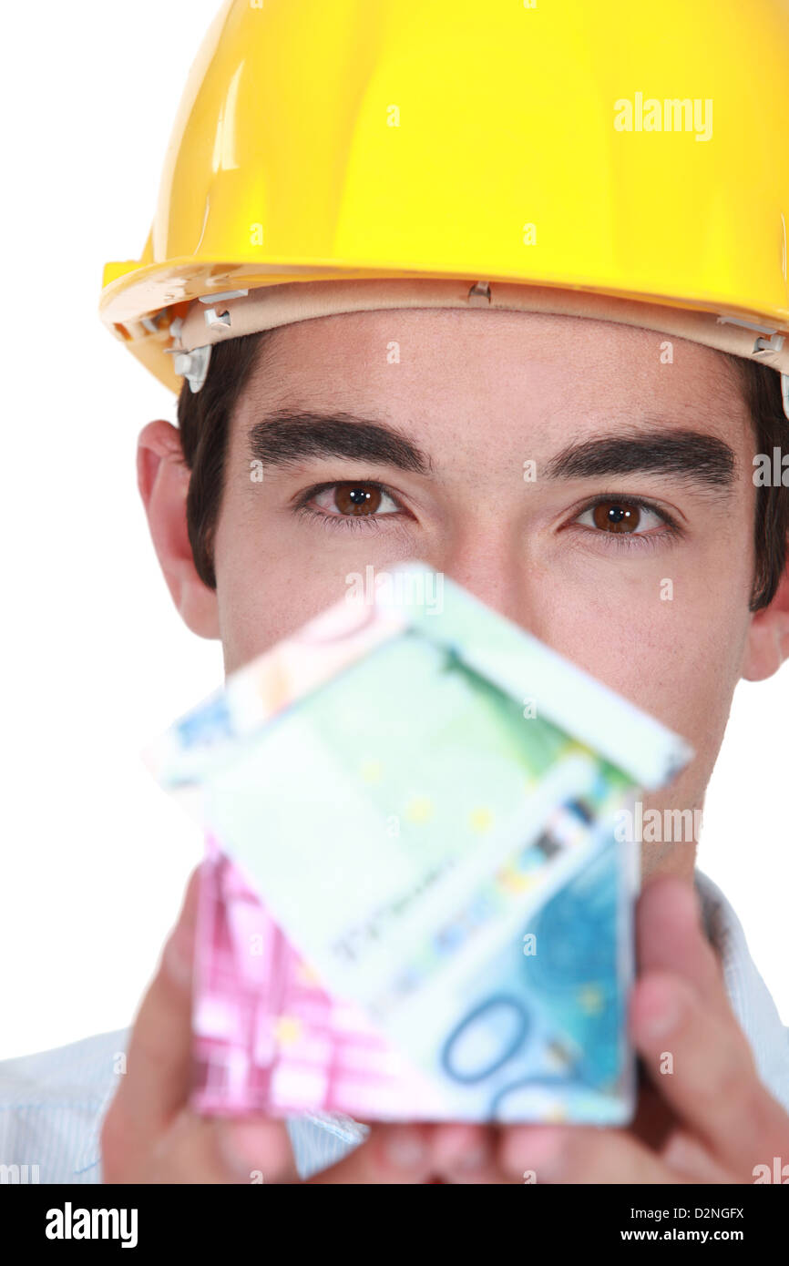 Construction worker holding house made from money Stock Photo - Alamy