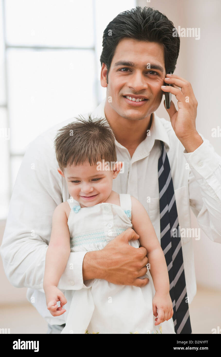 Man talking on a mobile phone and carrying his daughter Stock Photo - Alamy