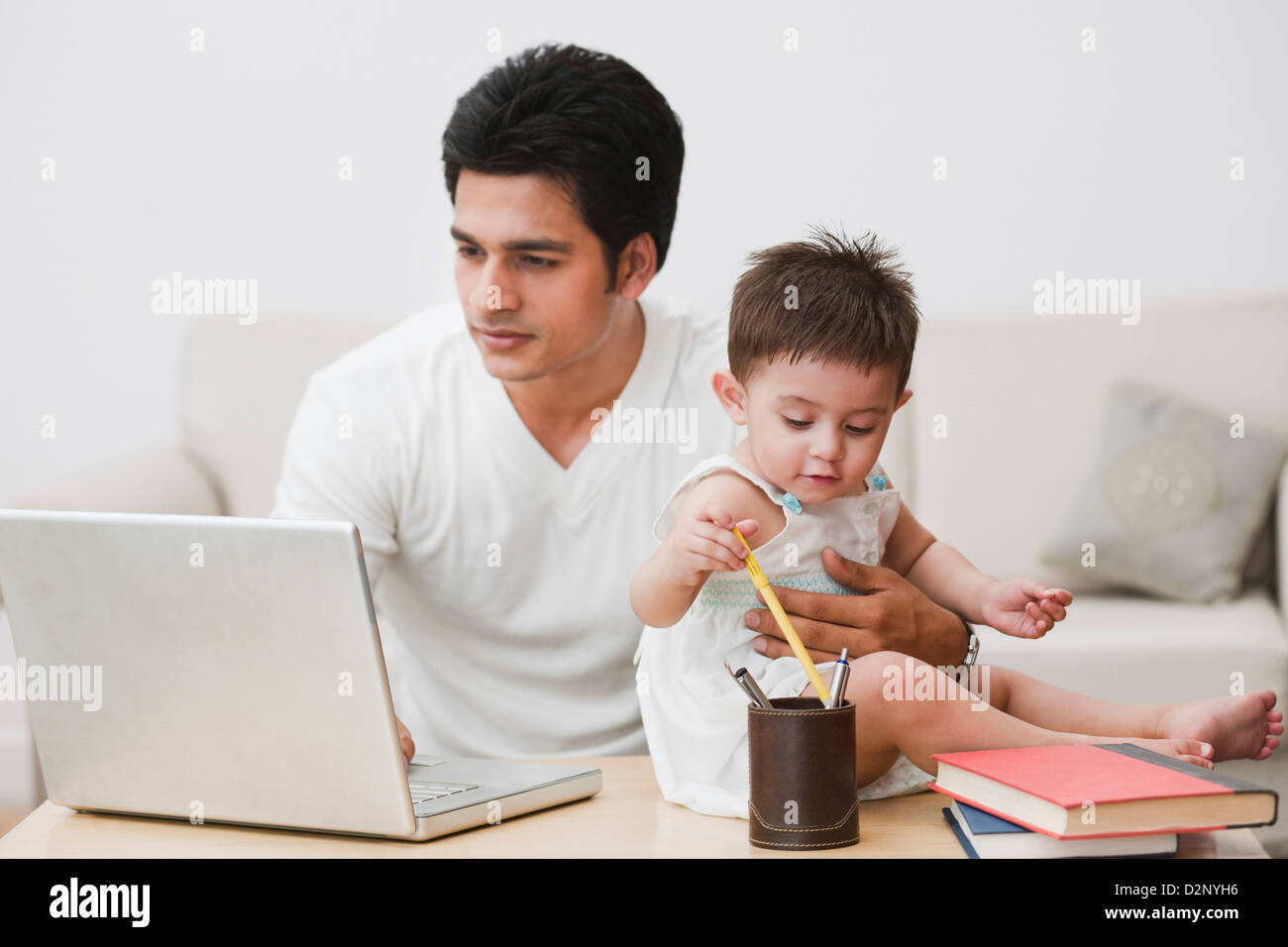 Man working on a laptop with his daughter sitting on a table Stock ...