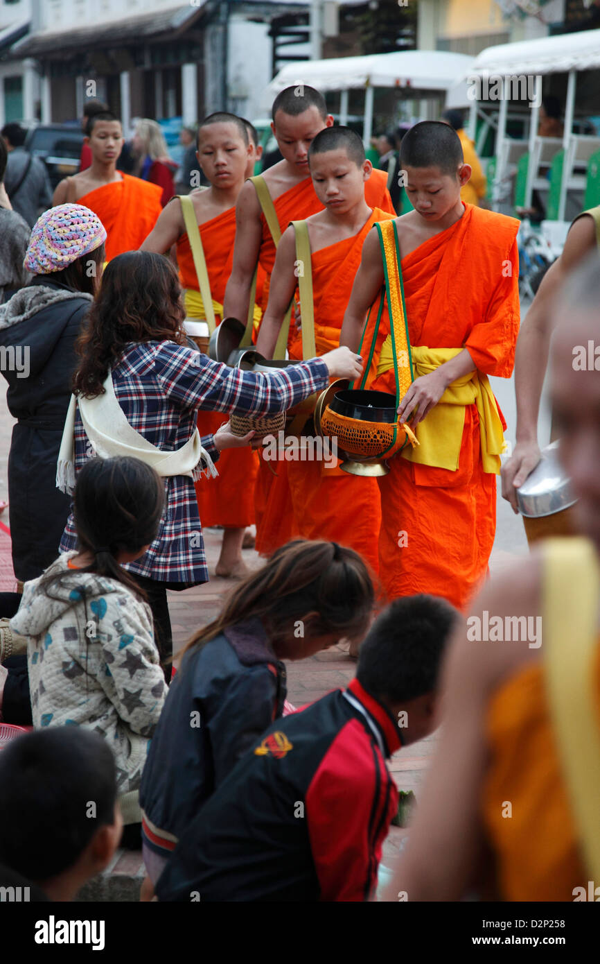 Monks wearing traditional saffron robes receiving alms at daybreak ...