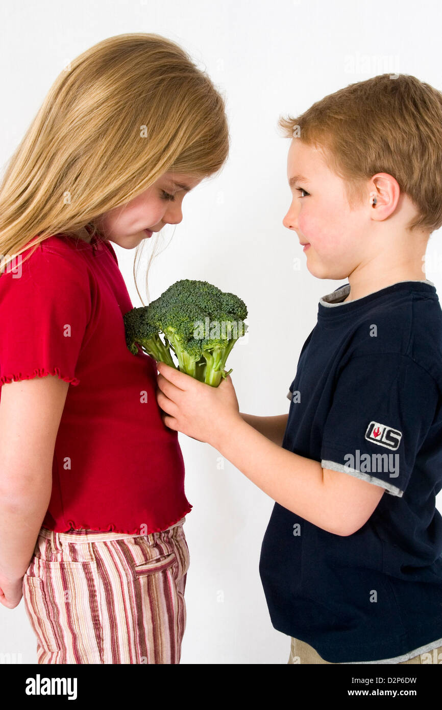 Young healthy children playing with a head of green broccoli. Boy gives ...