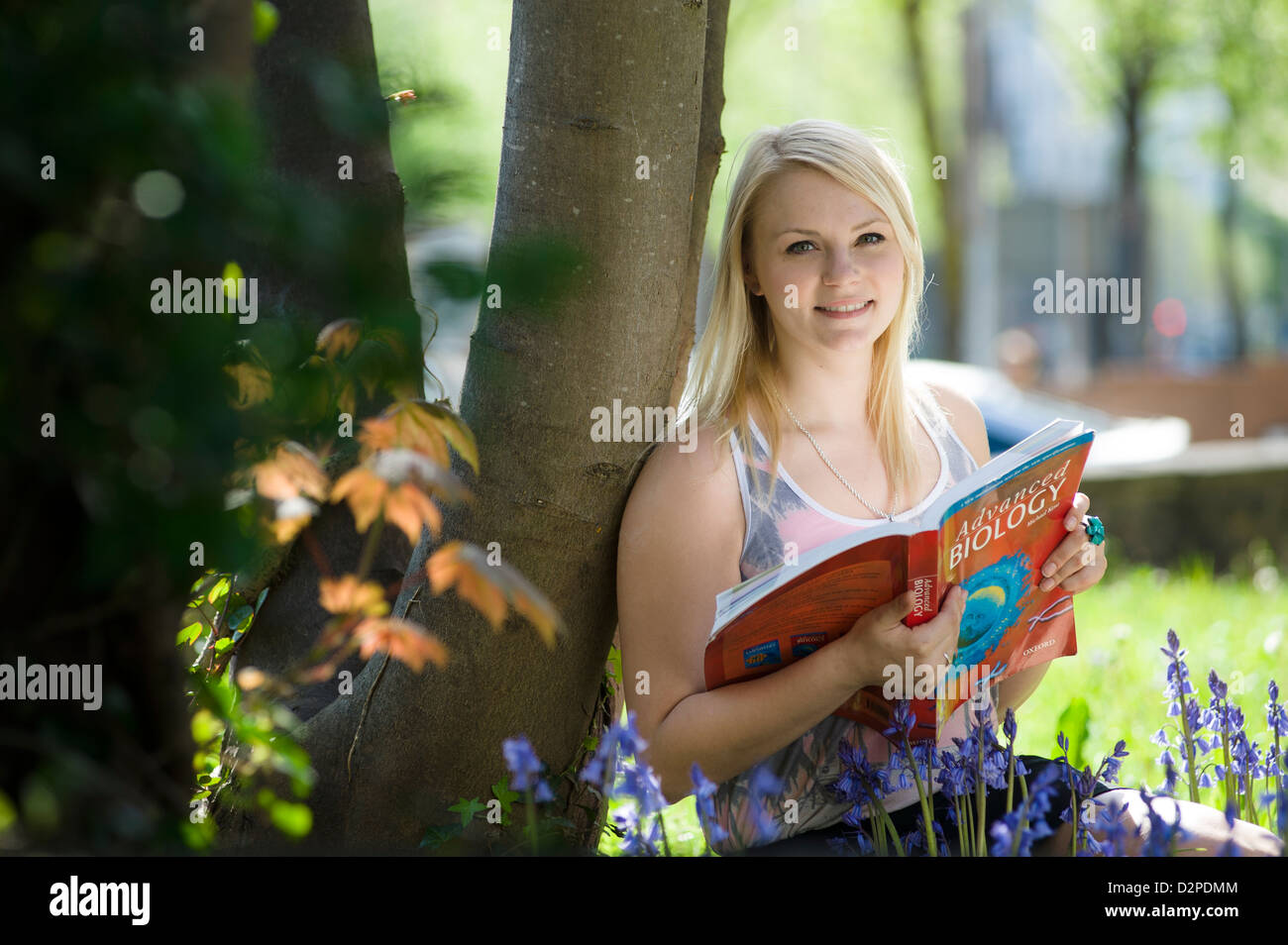 Young blond teenage girl studying and enjoying the day under the shade ...