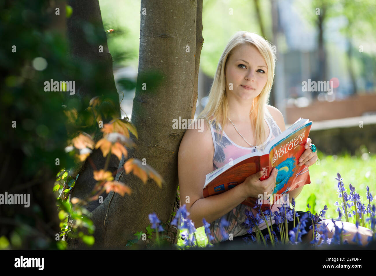 Young blond teenage girl studying and enjoying the day under the shade ...
