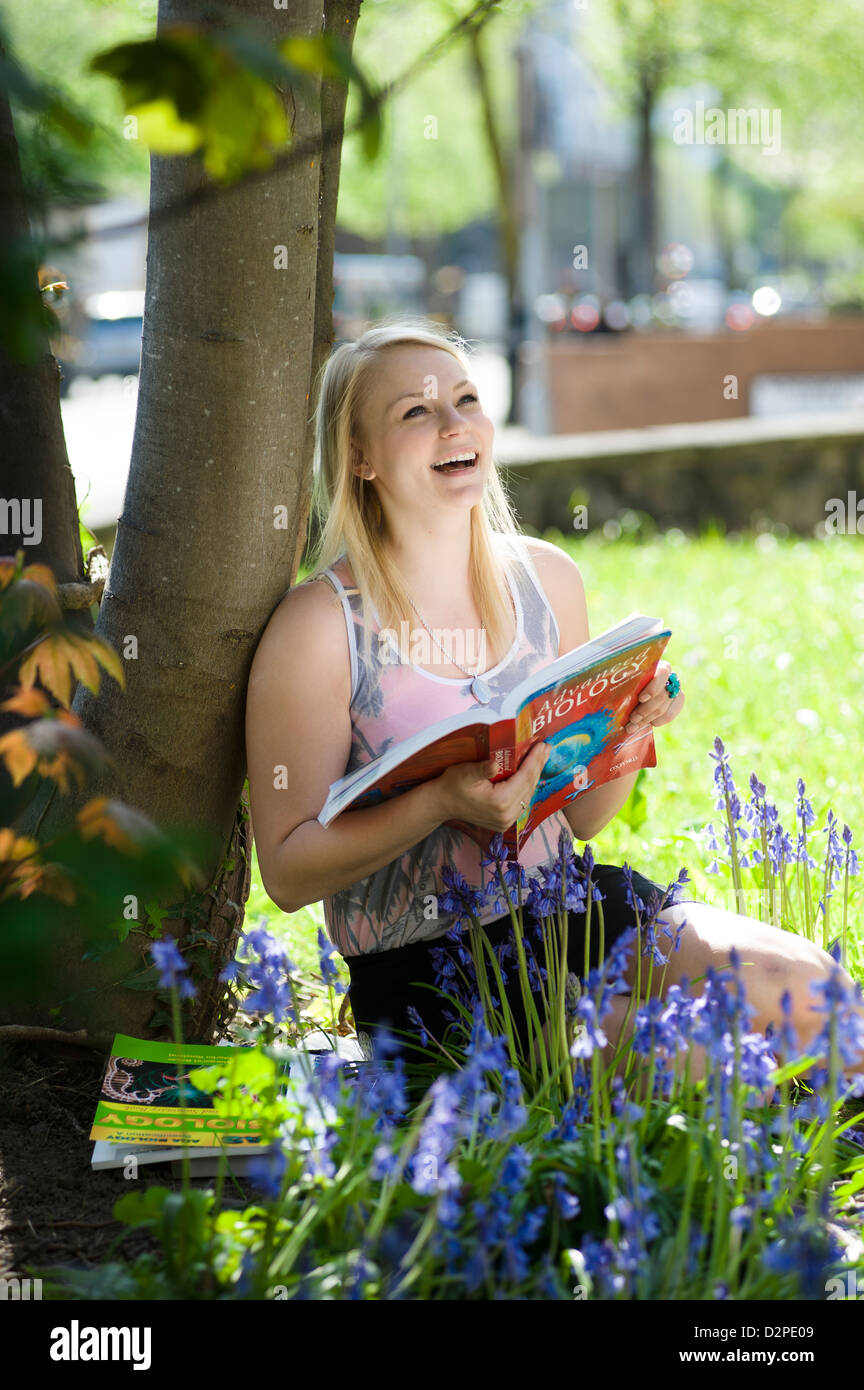 Young blond teenage girl studying and enjoying the day under the shade ...