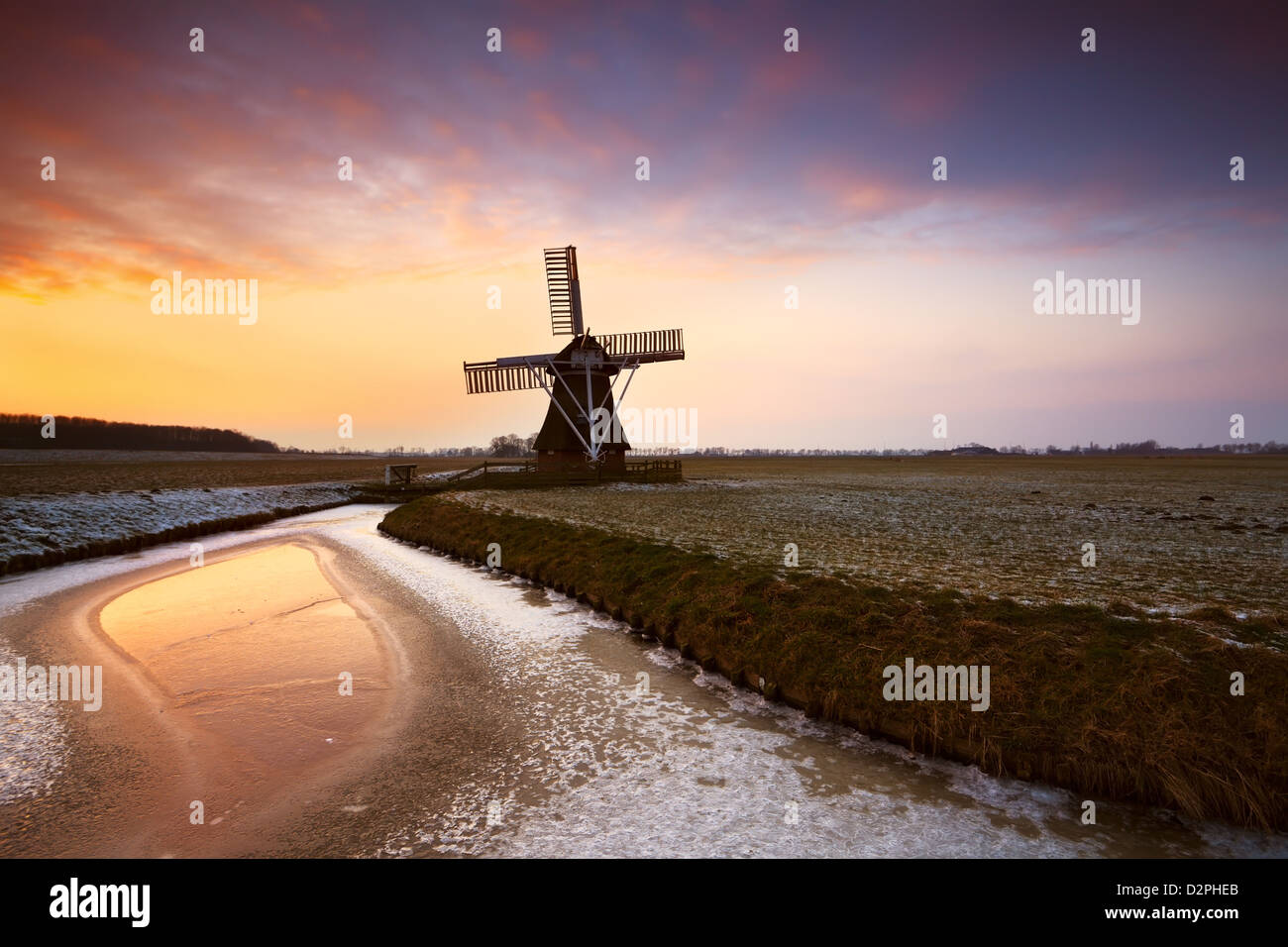 Dutch windmill by frozen canal at sunset Stock Photo - Alamy