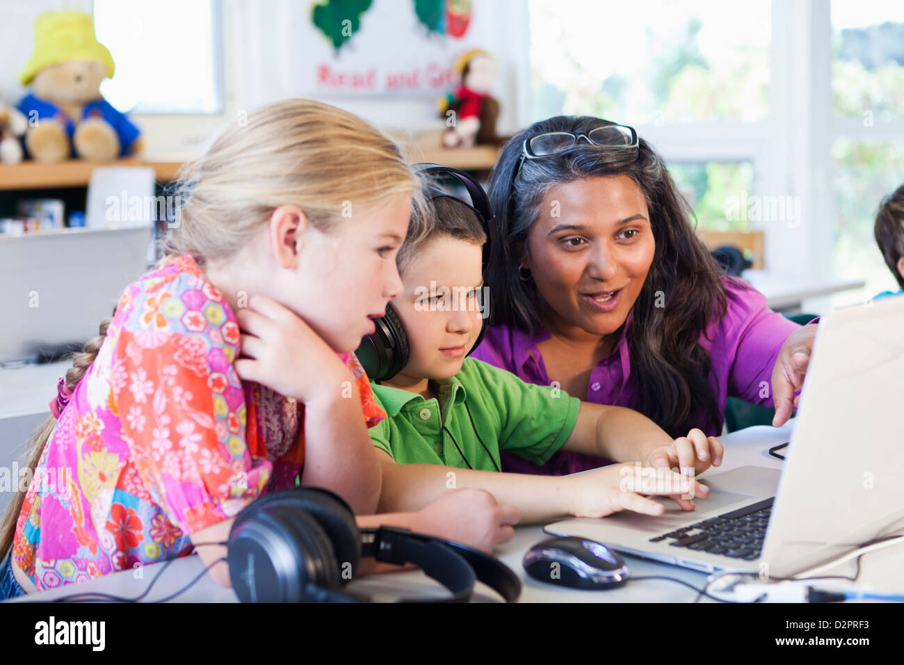 Teacher helping students using laptop Stock Photo - Alamy