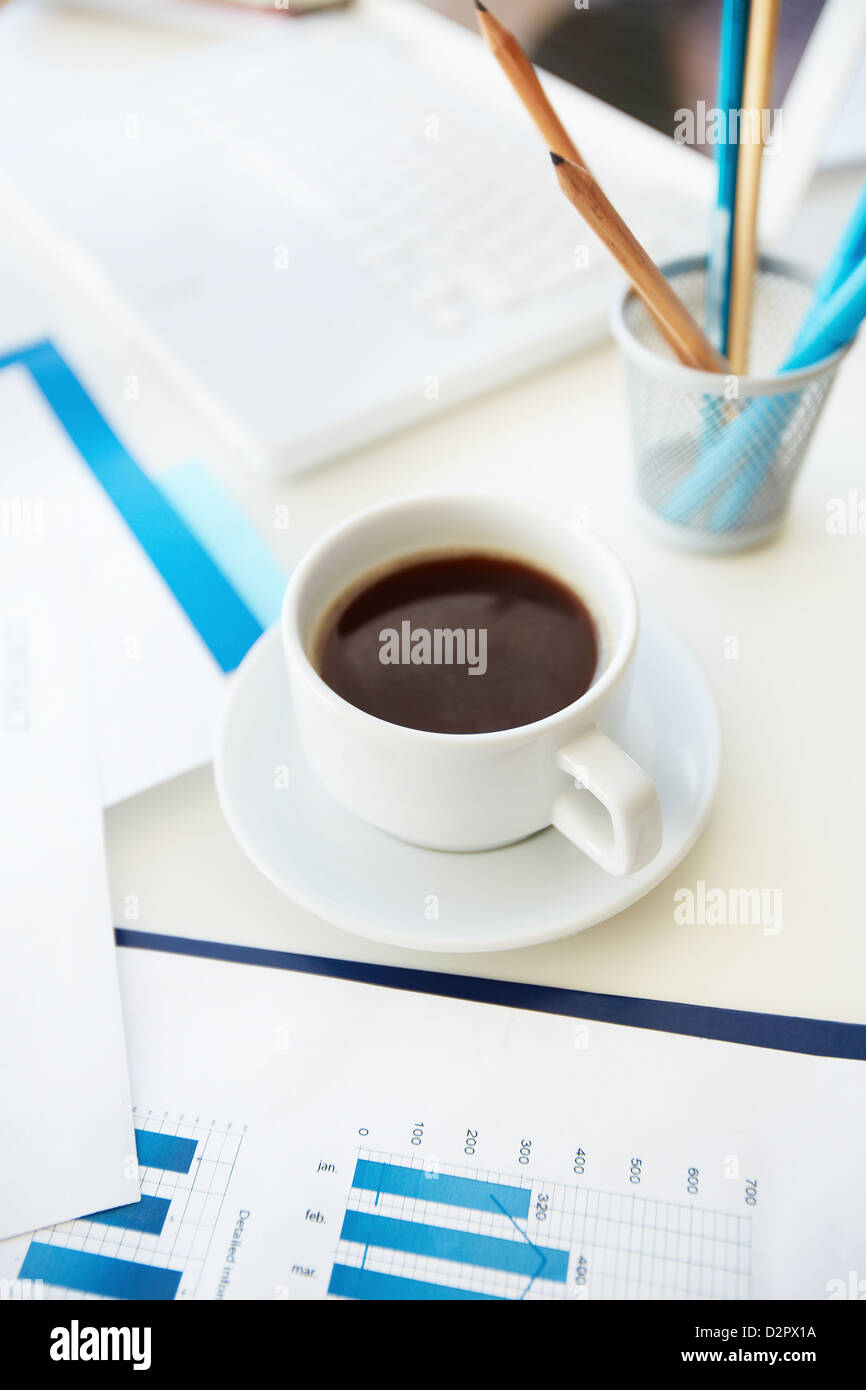 Vertical image of an office workplace with papers, stationary and a cup ...