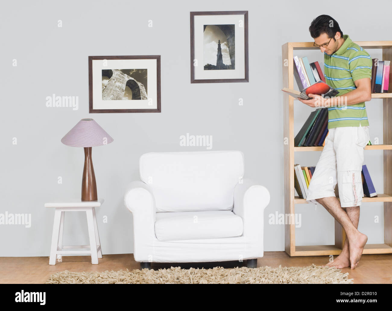 Man leaning against a bookshelf and reading a book Stock Photo - Alamy