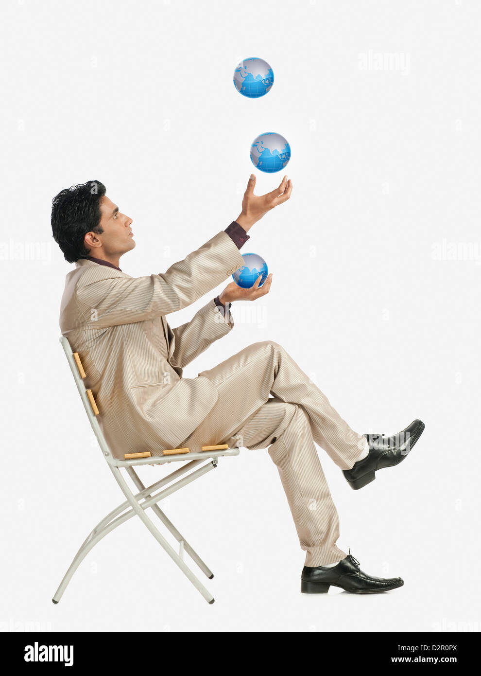 Businessman sitting on a chair and juggling globes Stock Photo - Alamy