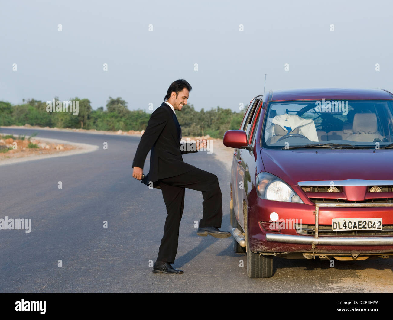 Businessman kicking a broken down car at the roadside Stock Photo - Alamy